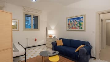 Um quarto com uma cama, um sofá azul, uma mesinha, um abajur, um quadro e uma janela.