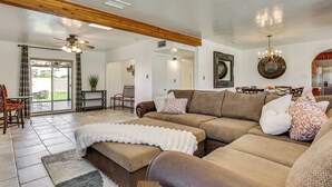 Uma sala de estar espaçosa com um sofá seccional grande, um ventilador de teto e um canto de jantar com mesa e cadeiras.
