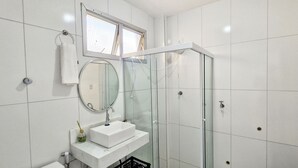 Casa de banho moderna com cabine de chuveiro em vidro, lavatório branco com espelho e porta-toalhas.