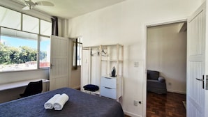 Quarto de hotel com cama, escrivaninha, cadeira, guarda-roupa e vista para o exterior.