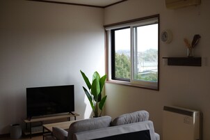 Quarto com cama, televisão em móvel, planta em vaso, janela com vista e radiador.