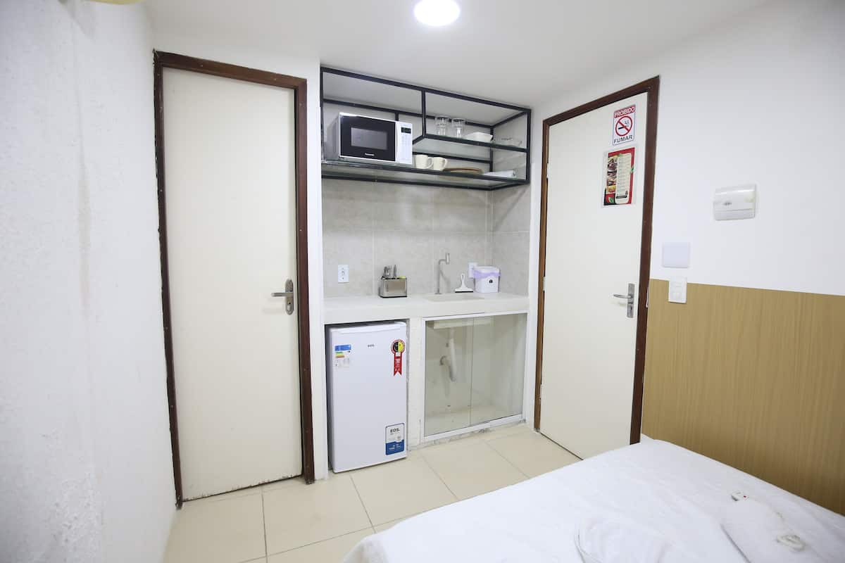 Quarto de hotel com cama, micro-ondas, frigorífico, armário envidraçado e porta com placa de 'Não Fumar'.