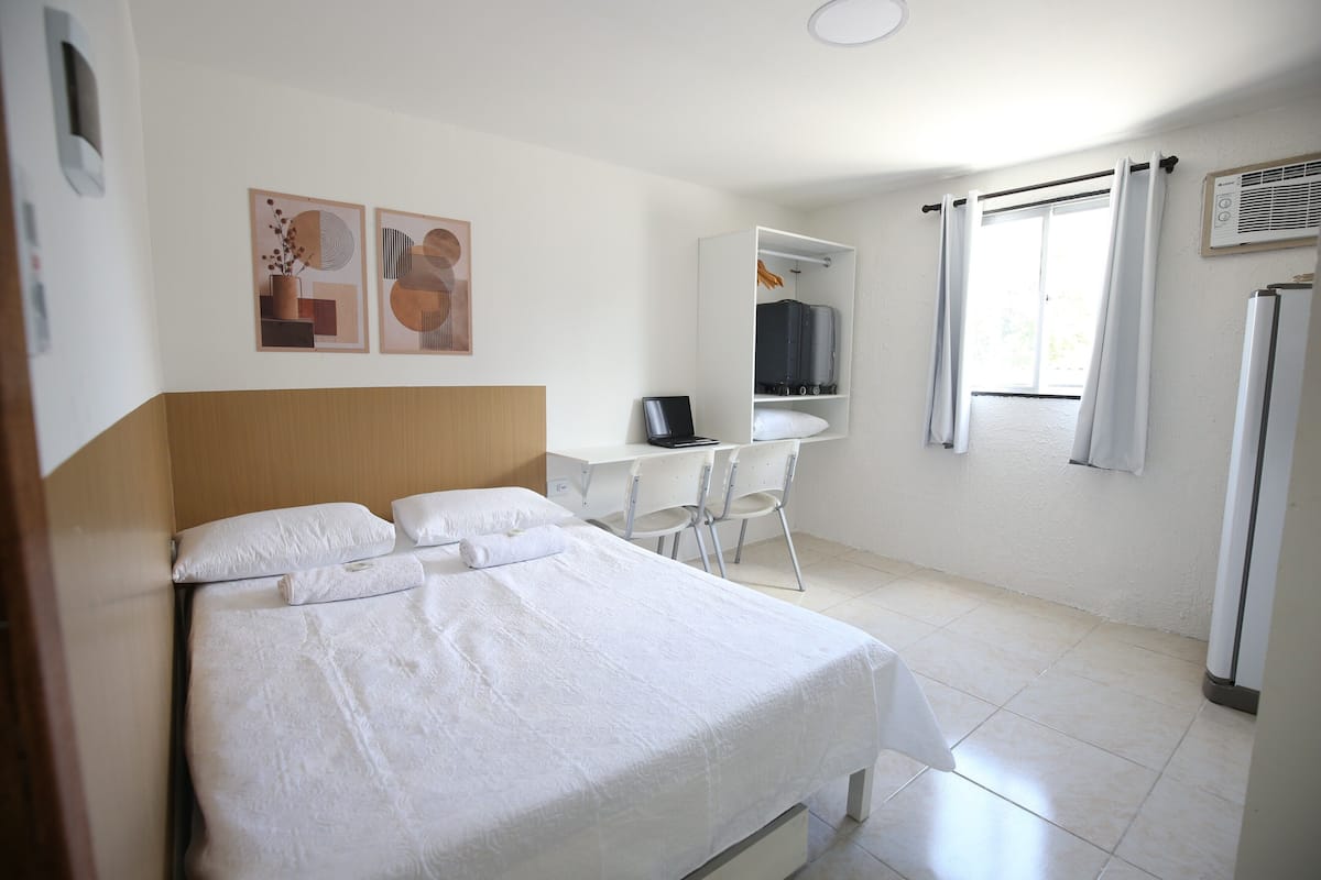 Quarto de hotel com uma cama, uma escrivaninha, cadeiras, um guarda-roupa e obras de arte na parede.