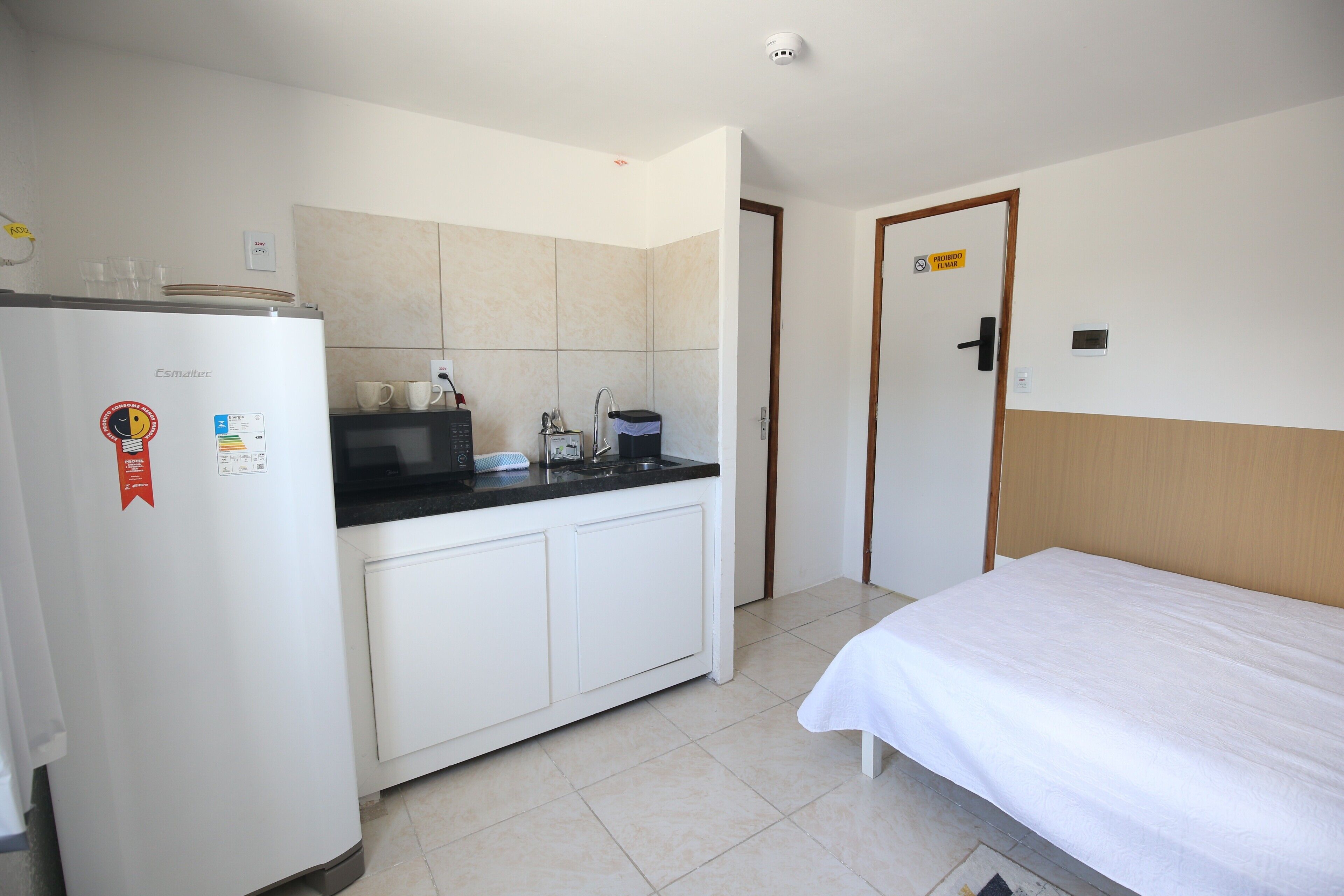 Quarto de hotel pequeno com cozinha compacta, uma cama e uma porta com o aviso 'Não Perturbe'.