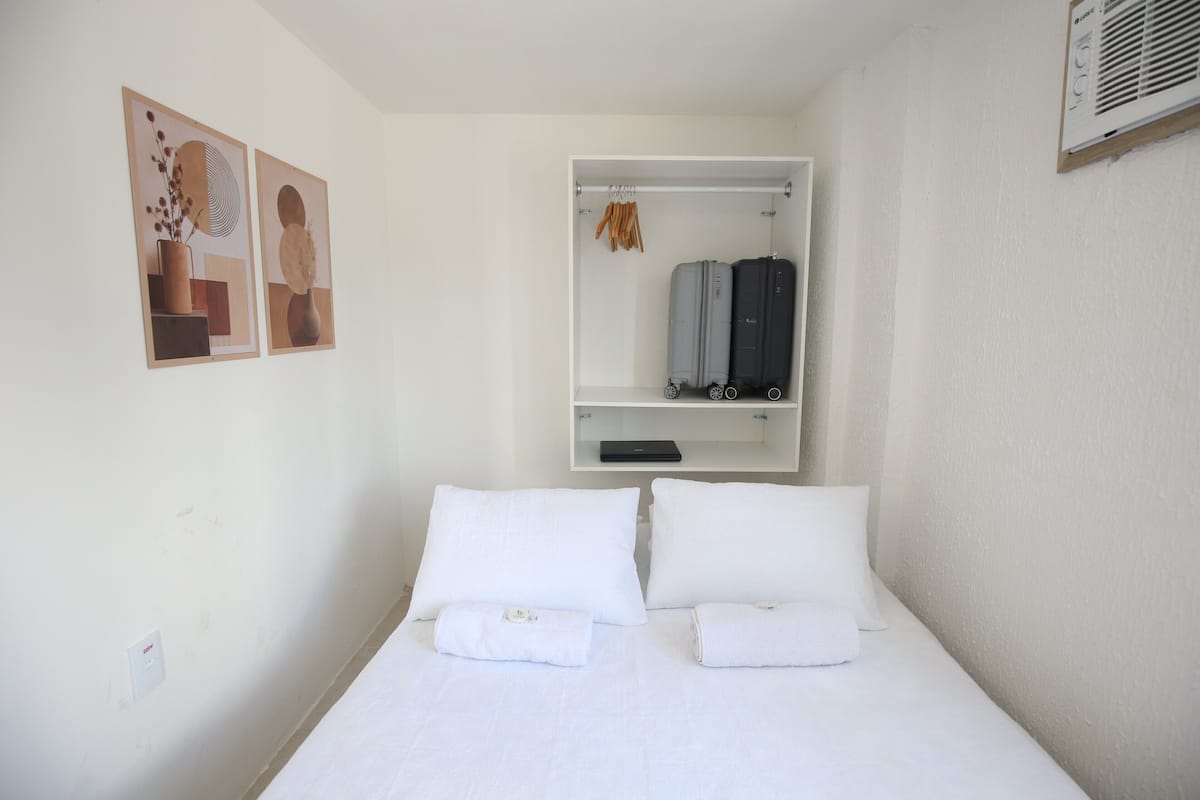 Quarto de hotel com cama, almofadas brancas, guarda-roupa e duas obras de arte na parede.