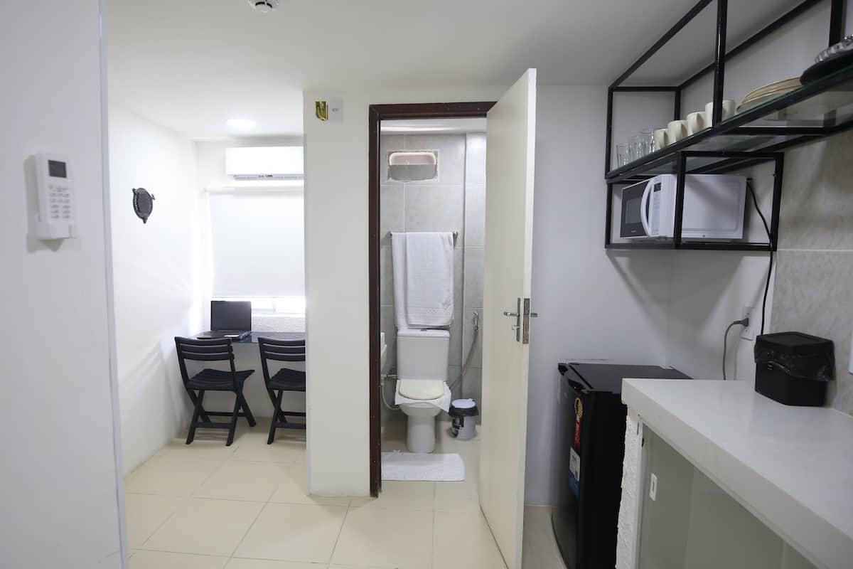 Casa de banho pequena e limpa, com sanita, lavatório e chuveiro. Há uma pequena mesa com um computador portátil e cadeiras.