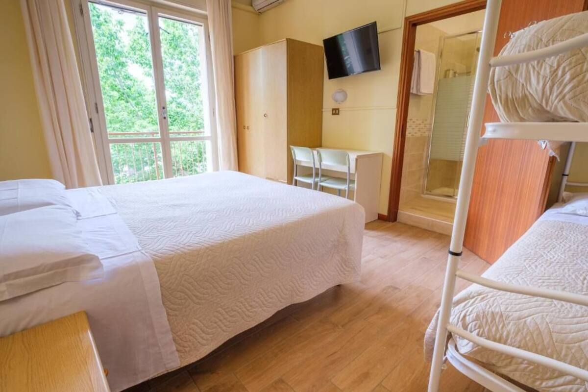Quarto de hotel com duas camas, uma escrivaninha, televisão e zona de chuveiro.