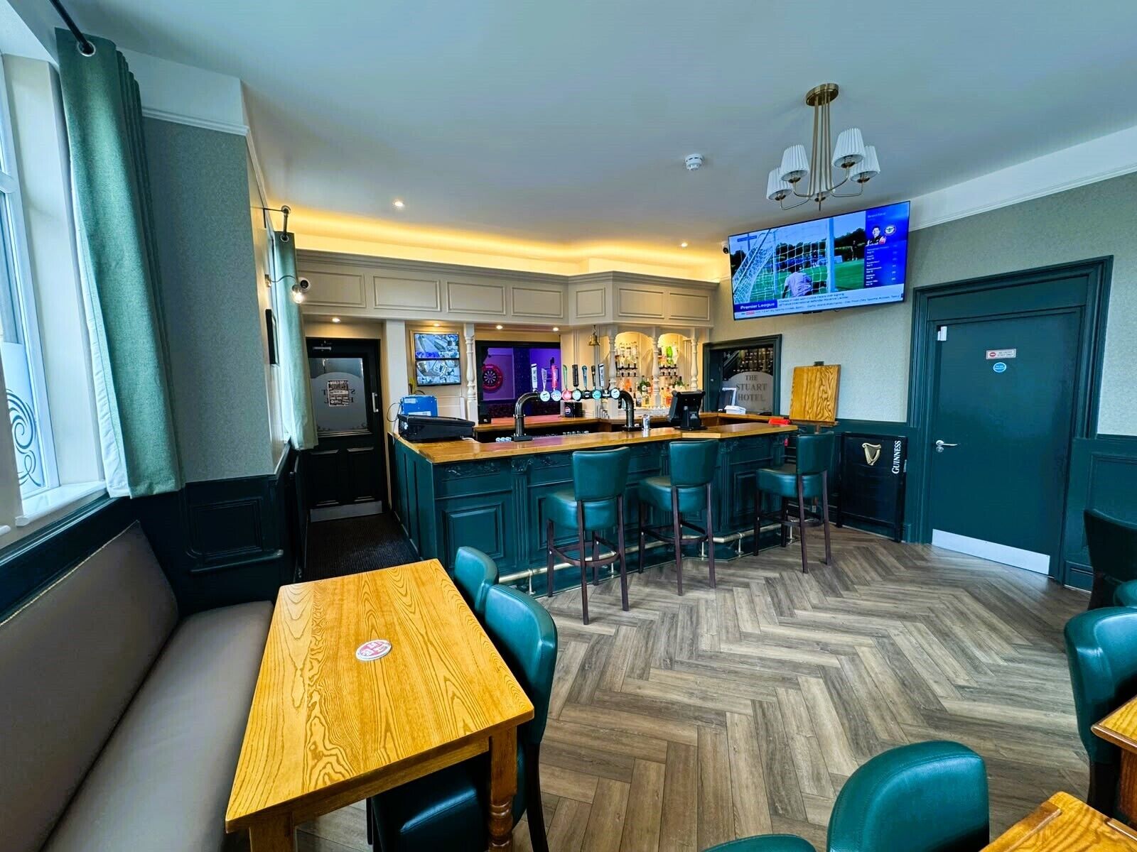 Um bar de hotel com balcão de madeira, banquetas e uma televisão na parede.