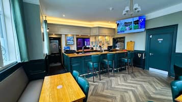 Um bar de hotel com balcão de madeira, banquetas e uma televisão na parede.