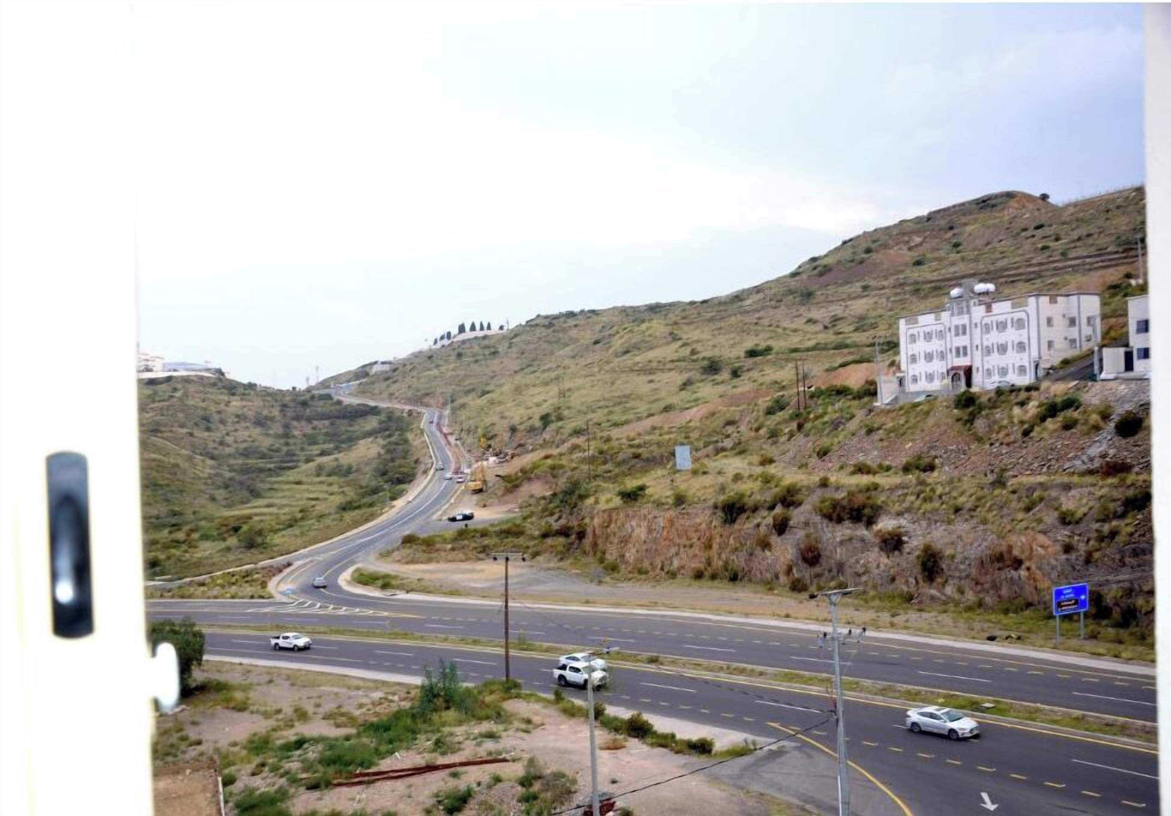 Uma estrada sinuosa serpenteando por uma paisagem montanhosa, com edifícios à direita.
