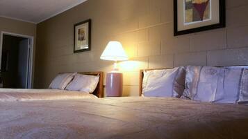 Quarto de hotel com duas camas, abajur, quadro na parede e uma porta à esquerda.
