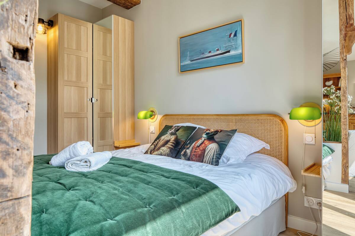 Quarto com colcha verde, pintura de um navio na parede e guarda-roupa de madeira.