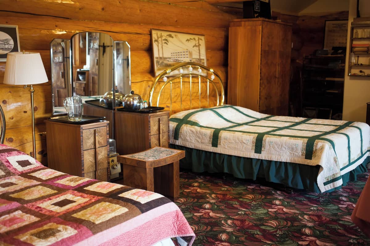 Quarto estilo cabana de madeira com uma cama, cômoda, espelho e uma pequena mesa.