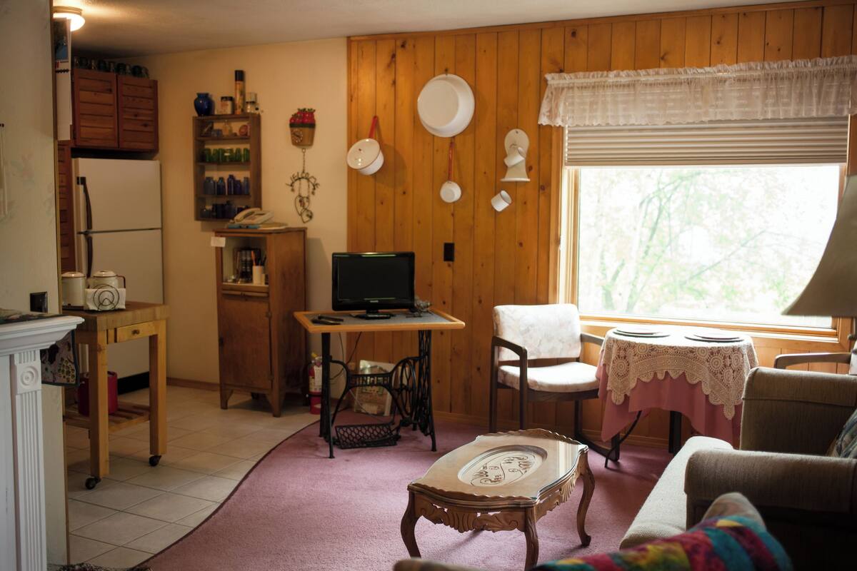 Uma sala de estar acolhedora com lareira, paredes de madeira, televisão e uma área de jantar com mesa e cadeiras.