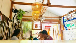 Interior de restaurante com vigas de madeira, luminárias pendentes, um ventilador e um mapa na parede.