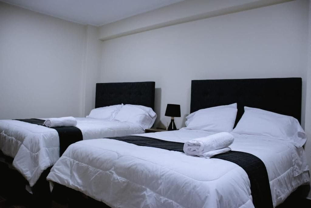 Duas camas de solteiro com roupa de cama branca e cabeceiras pretas em um quarto de hotel.