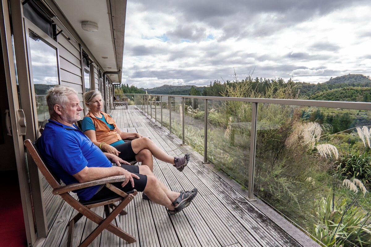 Um casal sentado em um deck de madeira com vista para uma paisagem arborizada.