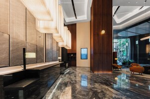 Um lobby moderno com piso de mármore, painéis de madeira e uma área de estar com cadeiras laranja.