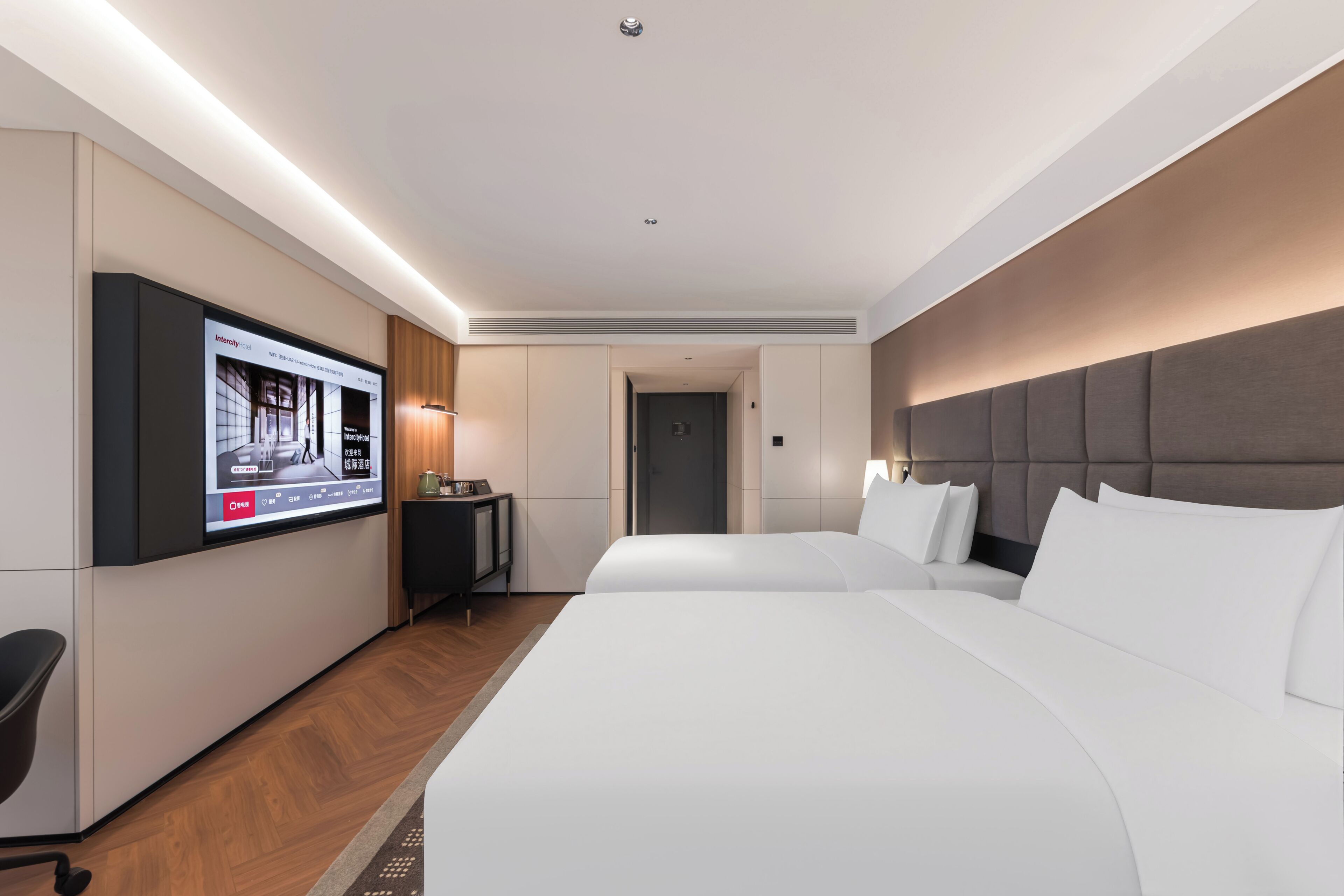 Quarto de hotel moderno com uma cama grande, televisão fixada na parede, uma mesa de trabalho e uma cadeira.