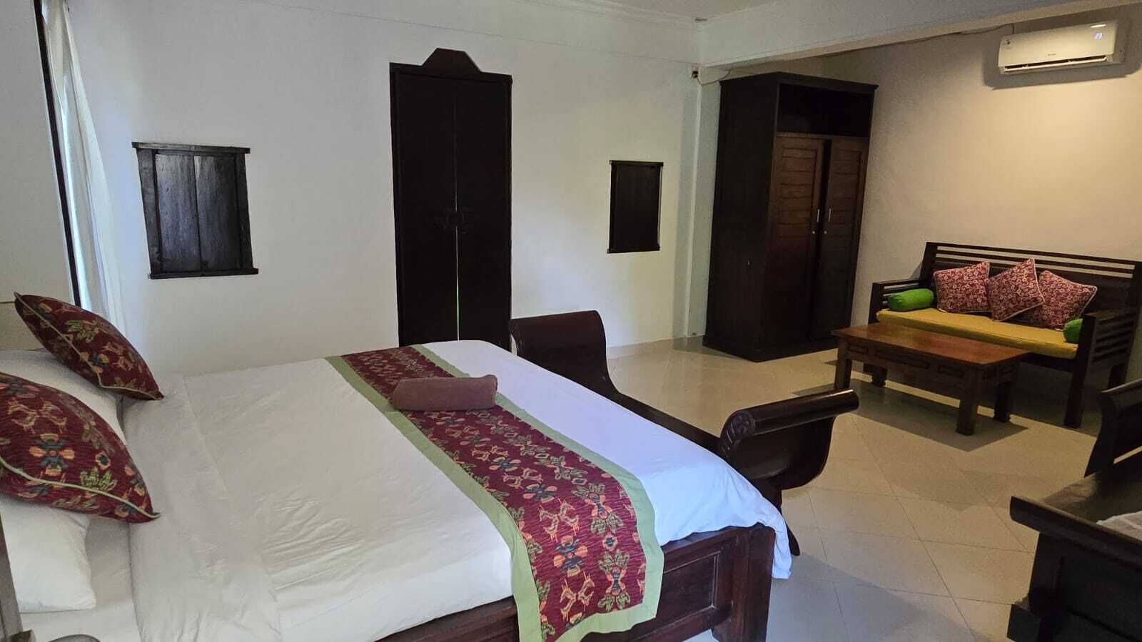 Quarto de hotel com uma cama grande, um banco de madeira e uma pequena mesa.