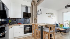 Uma cozinha moderna com armários brancos, forno embutido e uma área de jantar com cadeiras e mesa de madeira.