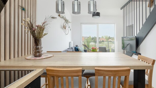 Uma área de refeições moderna com mesa de madeira, cadeiras estofadas cinzas e um vaso decorativo com plantas secas.