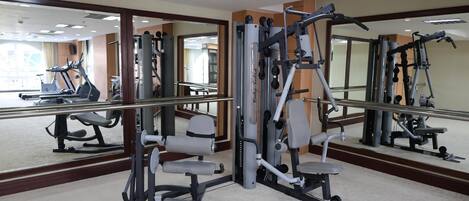 Uma academia com equipamentos de ginástica, espelhos e vista para o exterior.