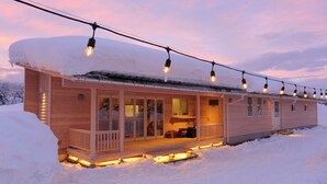 Uma cabana de madeira com varanda coberta, um pequeno deck e telhado coberto de neve.