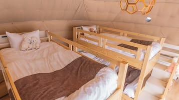 Um quarto tipo tenda aconchegante, com duas beliches, um ursinho de pelúcia na cama de baixo e um lustre pendurado.