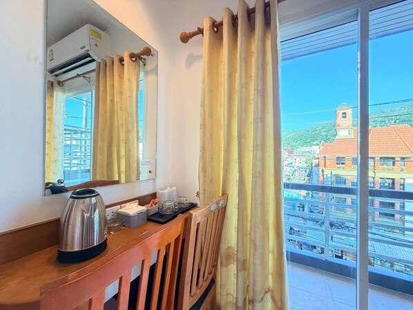Quarto com escrivaninha de madeira, chaleira e espelho refletindo uma vista urbana.