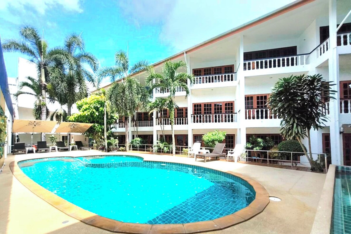 Hotel com piscina, várias varandas e palmeiras.