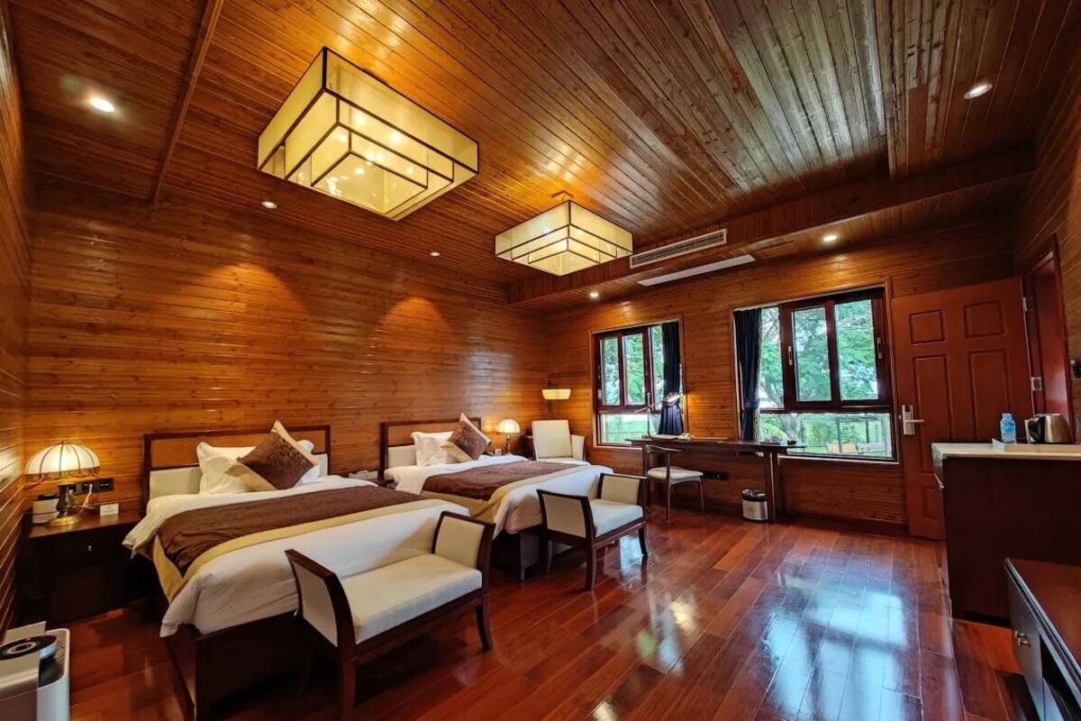 Quarto com painéis de madeira, duas camas, uma escrivaninha e vista para o exterior.