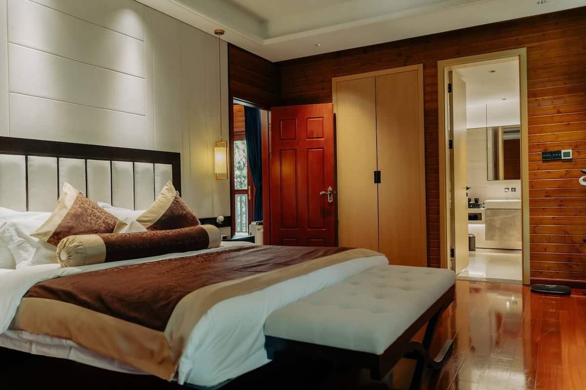 Quarto de hotel com uma cama grande, paredes de painel de madeira, uma porta vermelha e um banheiro visível.
