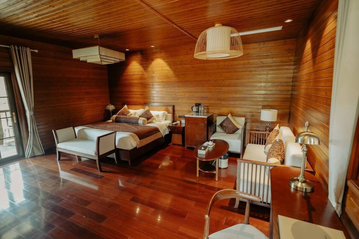 Quarto de hotel moderno com teto de madeira, uma cama grande, um sofá, uma escrivaninha e um abajur.
