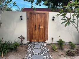Uma porta dupla de madeira com o número 5 na parede, rodeada por plantas e um caminho de pedra.