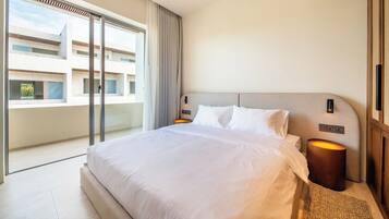 Quarto de hotel com uma cama grande, uma mesa de cabeceira, uma luminária e vista para um edifício por uma porta de correr.