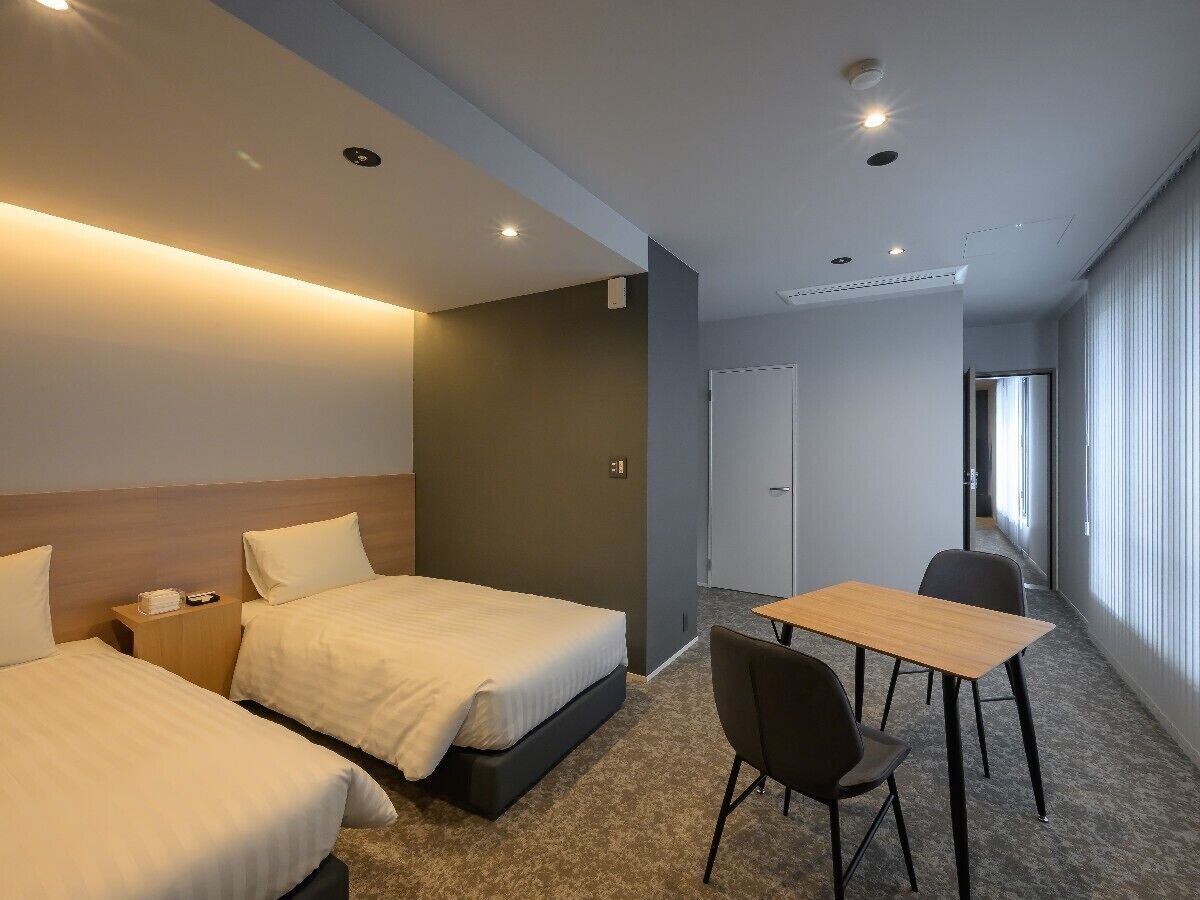 Quarto de hotel com duas camas, uma mesa e uma cadeira.