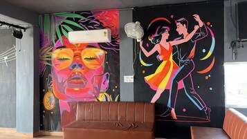 Um quarto com um mural colorido, um sofá de couro marrom e um ventilador de teto.