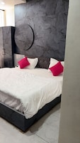 Cama com roupa de cama branca e duas almofadas cor-de-rosa, uma cabeceira escura e um adorno circular na parede.