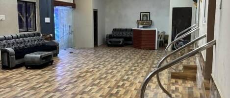 Um quarto amplo com piso de madeira estampado, um sofá, uma escrivaninha e uma escada com guarda-corpo de metal.