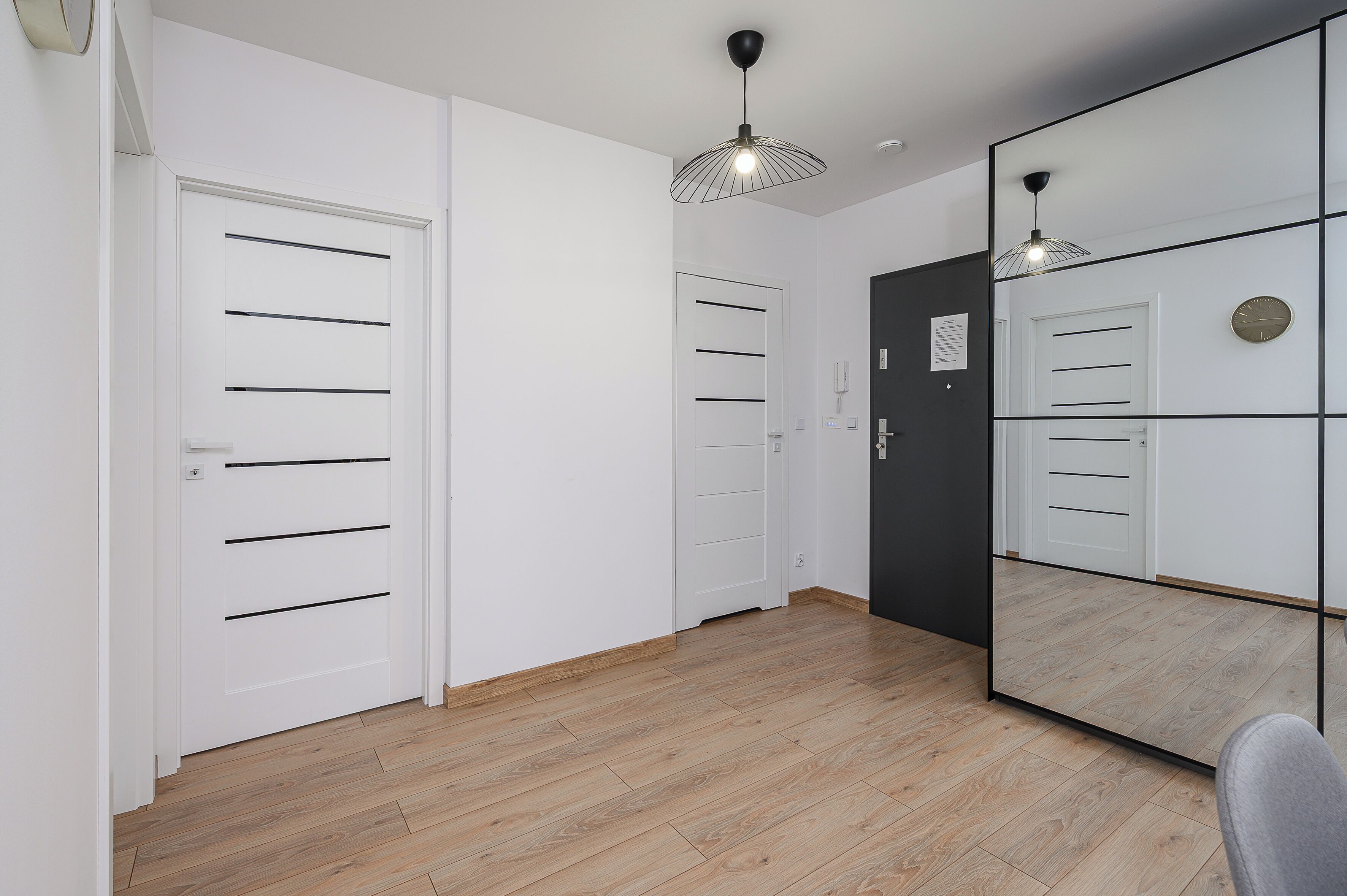 Um corredor com um guarda-roupa espelhado, uma porta com puxadores horizontais e um acessório de iluminação.