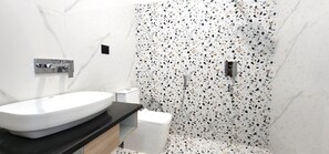 Casa de banho com lavatório branco, bancada preta, sanita branca e chuveiro com parede de azulejos salpicados.