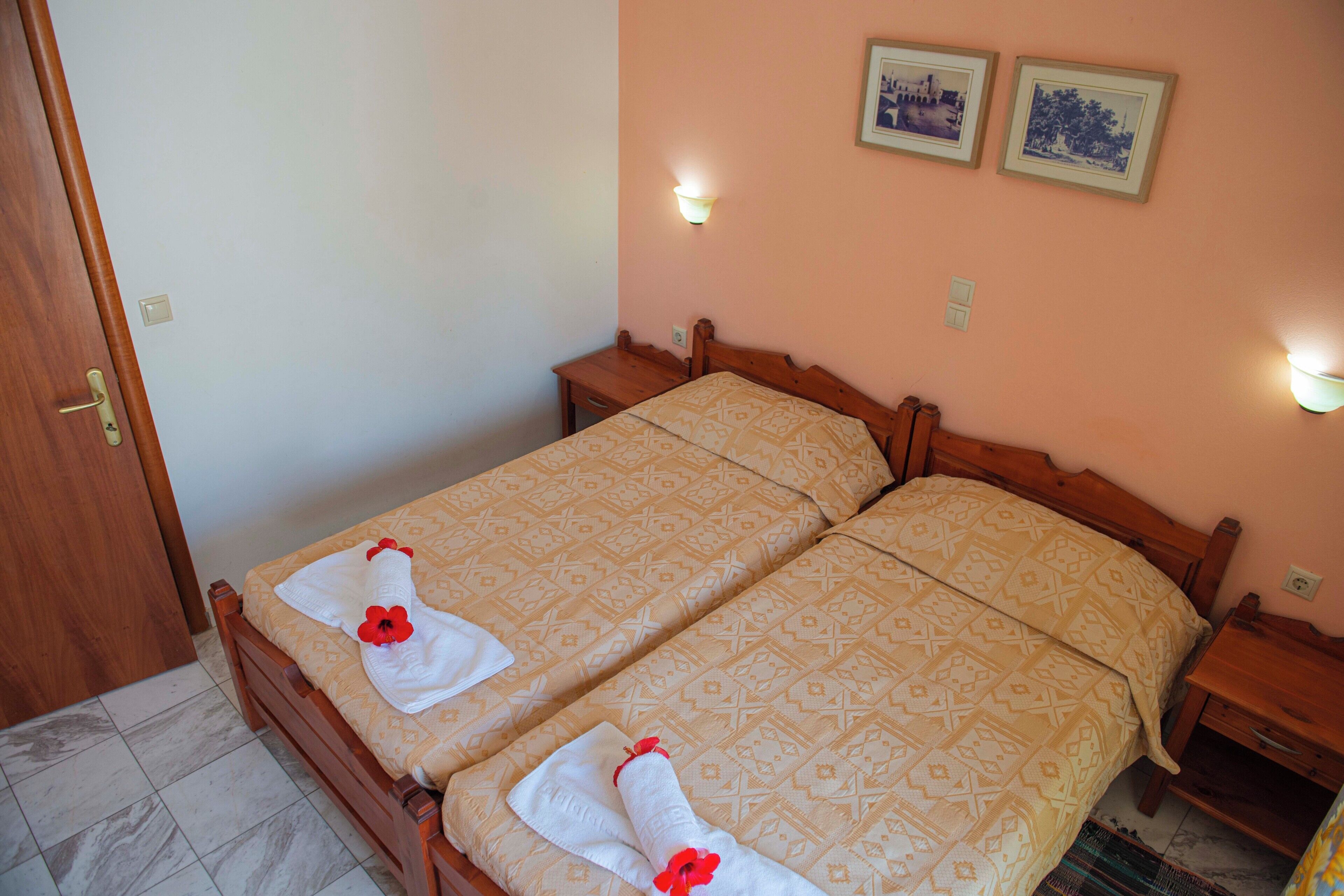 Uma cama de casal com roupa de cama estampada, duas mesas de cabeceira, uma luminária fixada na parede e dois quadros emoldurados.