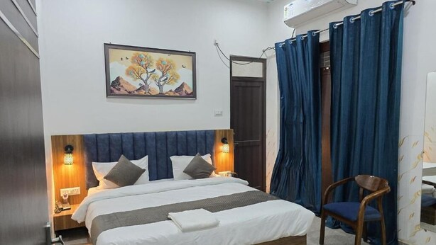 Quarto com cama, abajures, uma cadeira, um quadro e cortina.