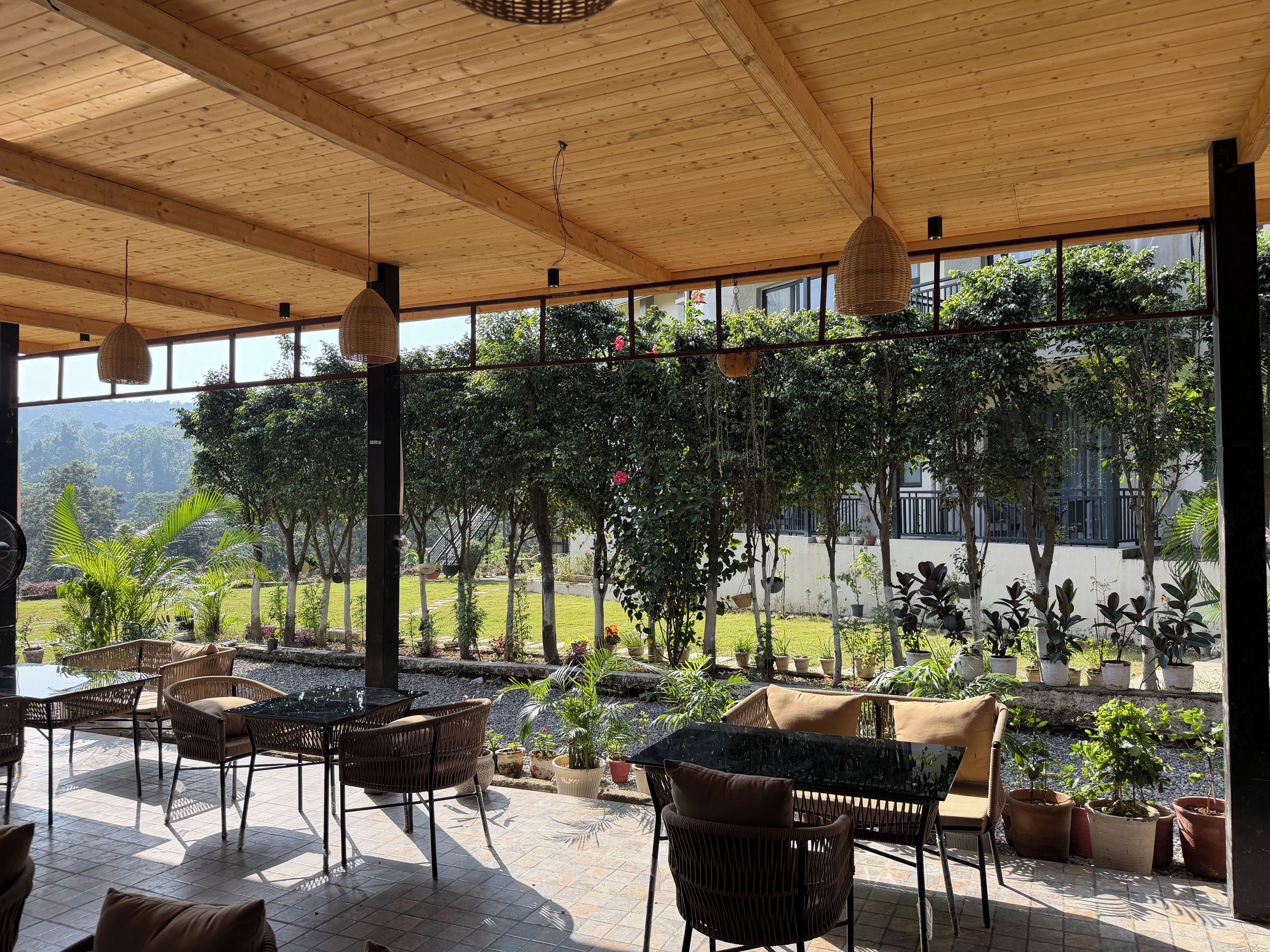 Espaço ao ar livre com mesas e cadeiras, cercado por plantas em vasos e árvores.