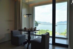 Quarto com mesa e cadeiras, vista para um corpo d'água e varanda.