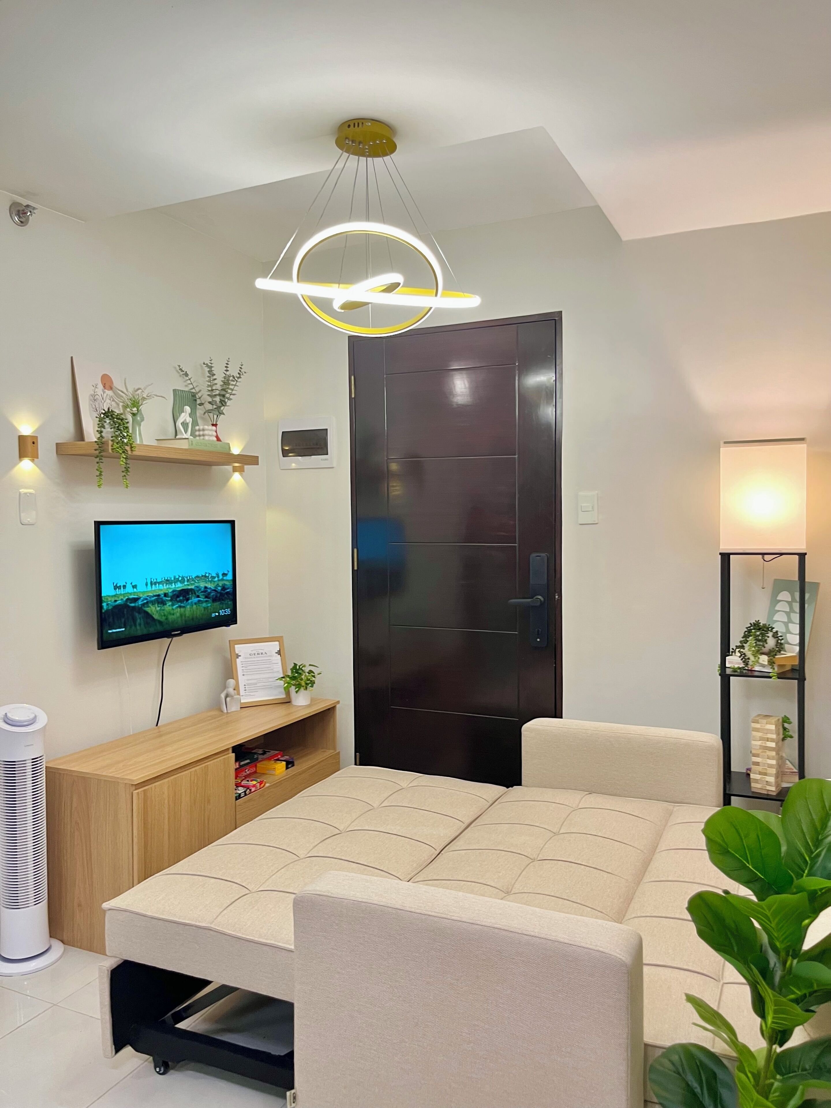 Uma sala de estar moderna com uma televisão de tela plana, um sofá, uma mesa de centro, uma luminária no teto e uma porta.