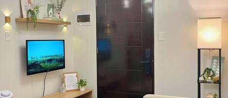 Uma sala de estar moderna com uma televisão de tela plana, um sofá, uma mesa de centro, uma luminária no teto e uma porta.