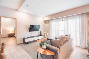 Uma sala de estar moderna com um sofá, mesa de centro, TV e uma grande janela com cortinas.