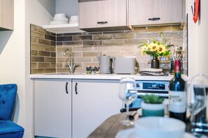 Cozinha moderna com painel de azulejos, armários brancos e bancada com cafeteira, torradeira e um vaso com flores.